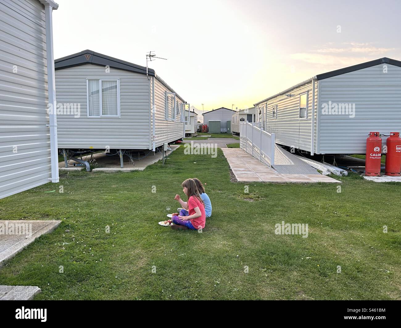 2 girls sit cross legged on the grass in the middle of a caravan park ...