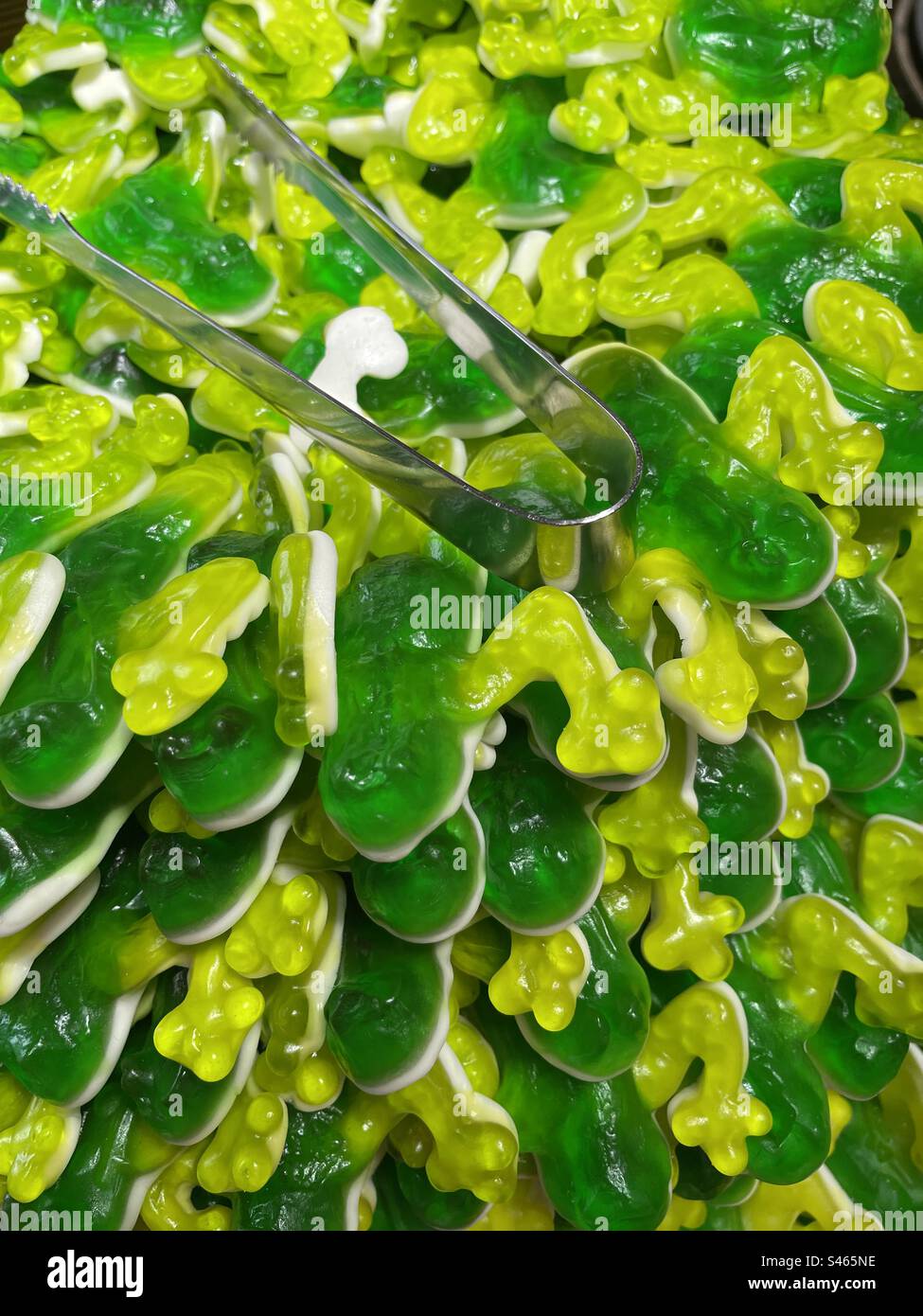 Green jelly frogs for sale in a pick and mix shop, with serving tongs ...