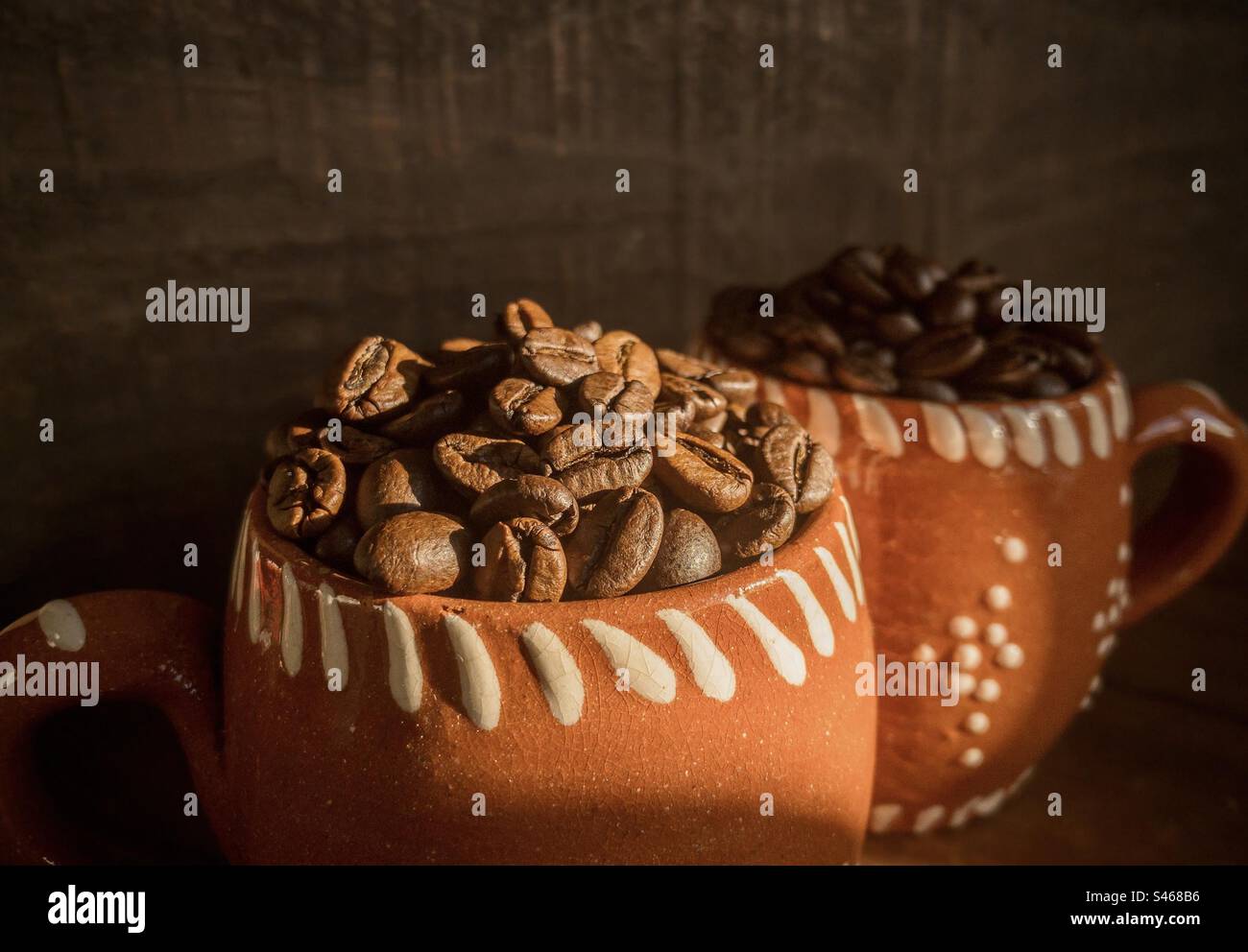 2 terracotta mugs filled with coffee beans caught in a shaft of ...