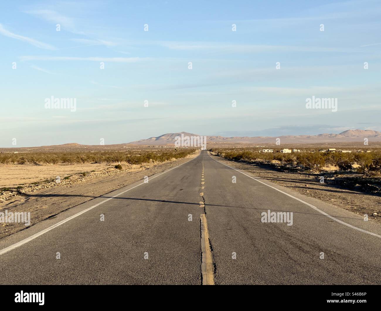 Desert road disappearing into the distance, with mountains visible and ...