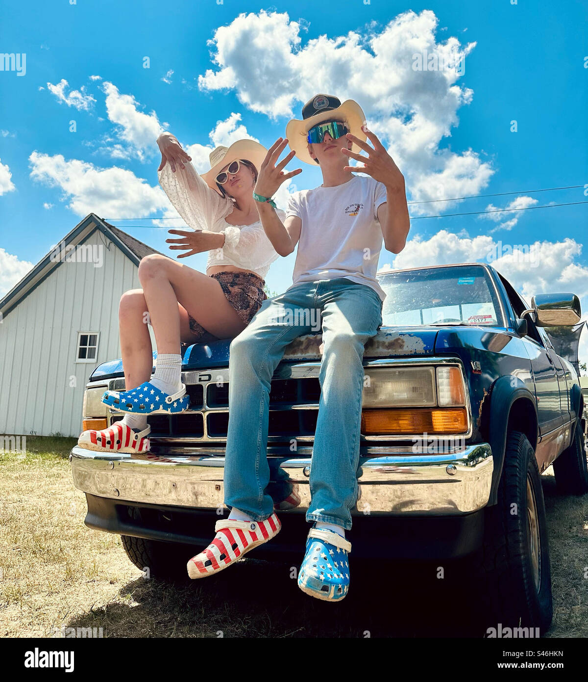Two young American teenagers sitting on the hood of an old pickup truck ...