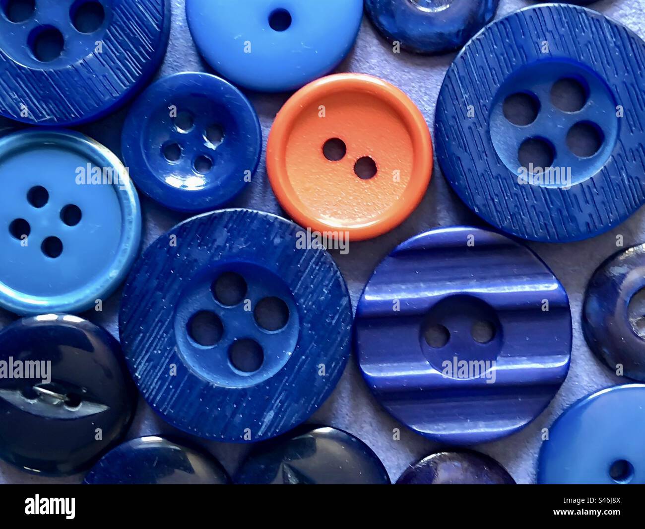 One orange button amongst assorted blue ones Stock Photo - Alamy