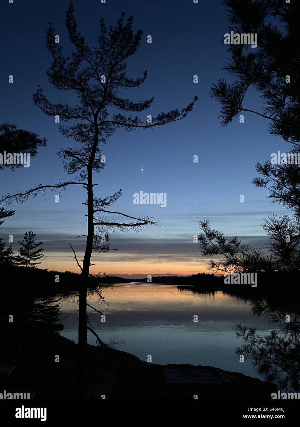 Night sky after sunset reflecting off water frames by trees Stock Photo ...