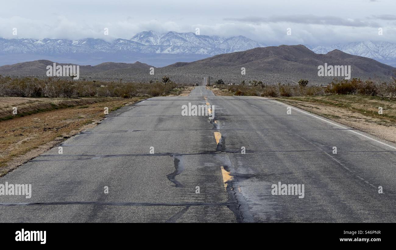Cracked and broken desert highway, leading straight to foothills and ...
