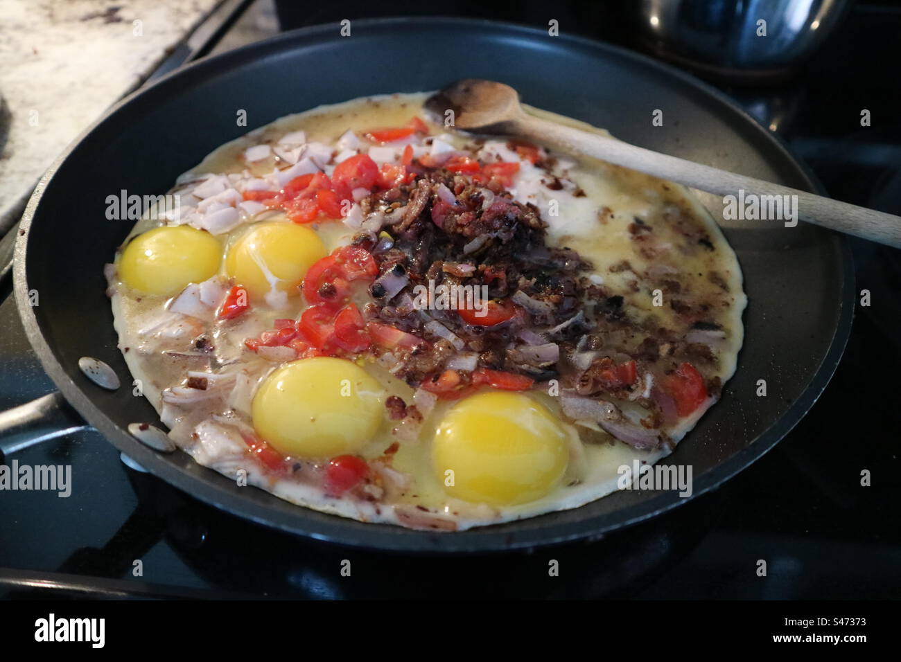 Breakfast omelet cooking in a pan on a stove with eggs and ham onion ...