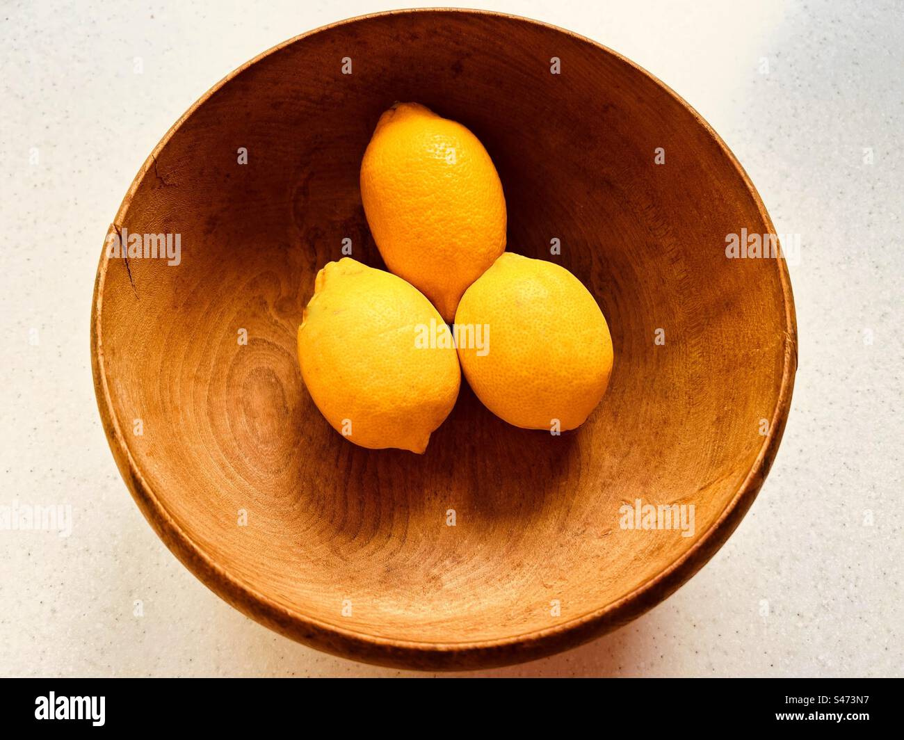Three yellow lemons in a grained wooden bowl. Acidic, bitter, sour ...
