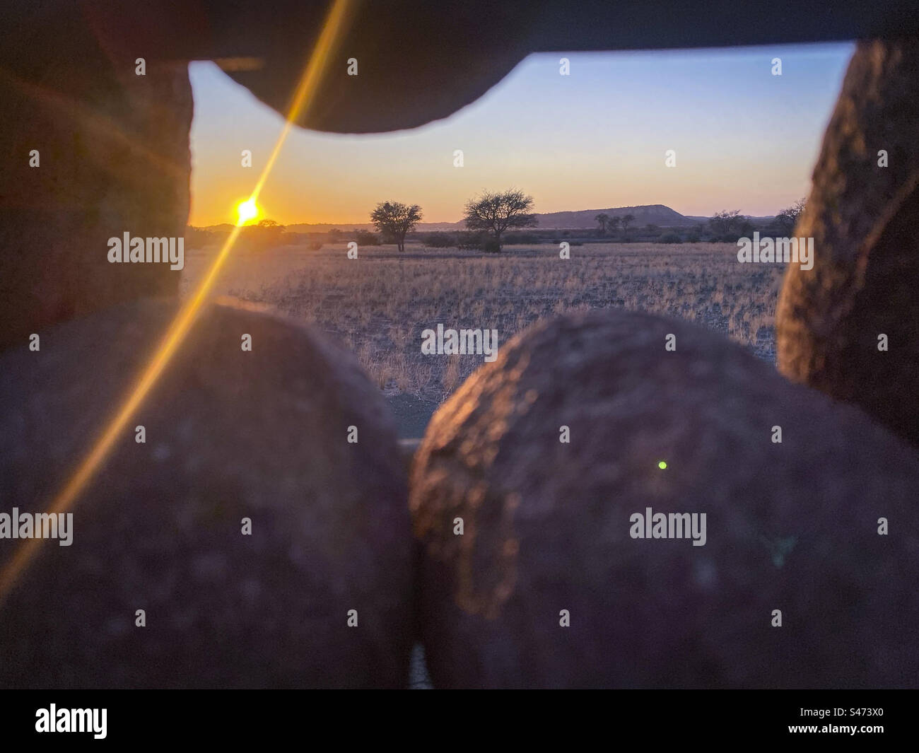 The sun rises through a fence made of round rocks in Southern Namibia ...