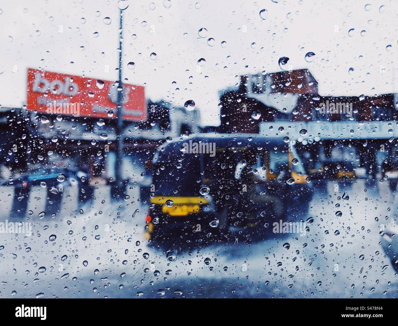 An auto rickshaw in the rain from a car window full of water droplets ...
