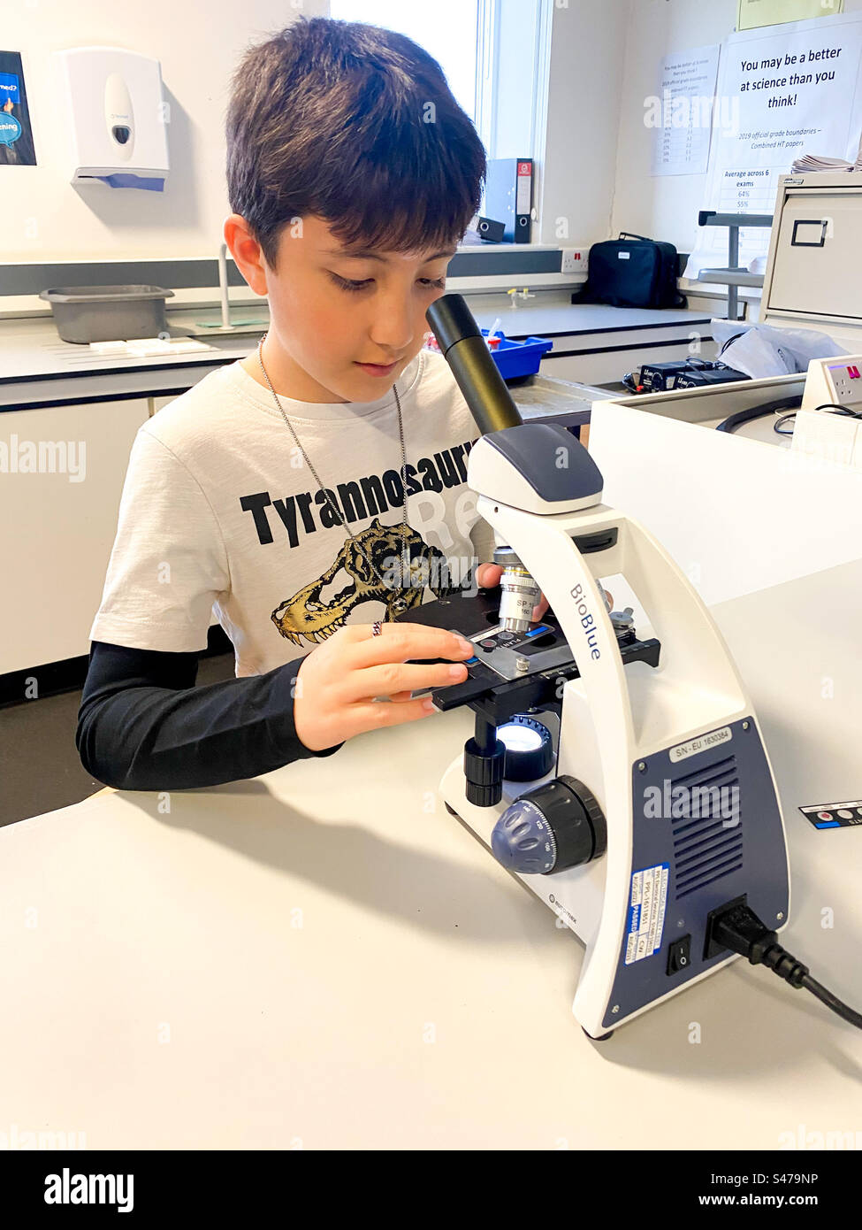 A boy looking at a sample under a microscope in a school science lab ...