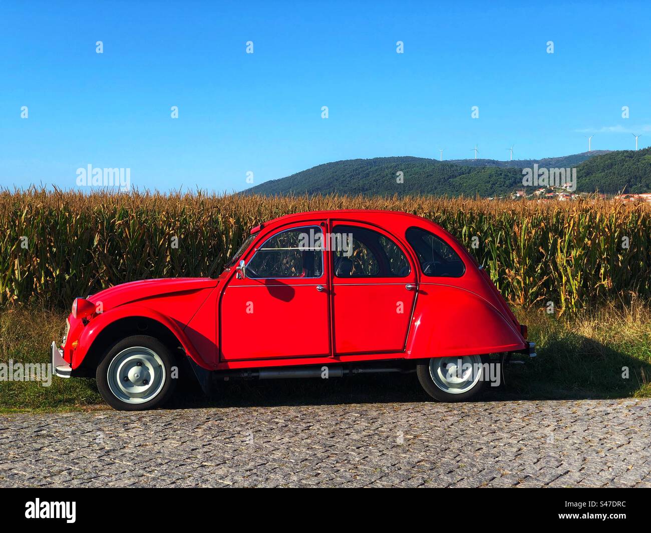 Red vintage Citroën car parked by the farm field with the hills on the ...