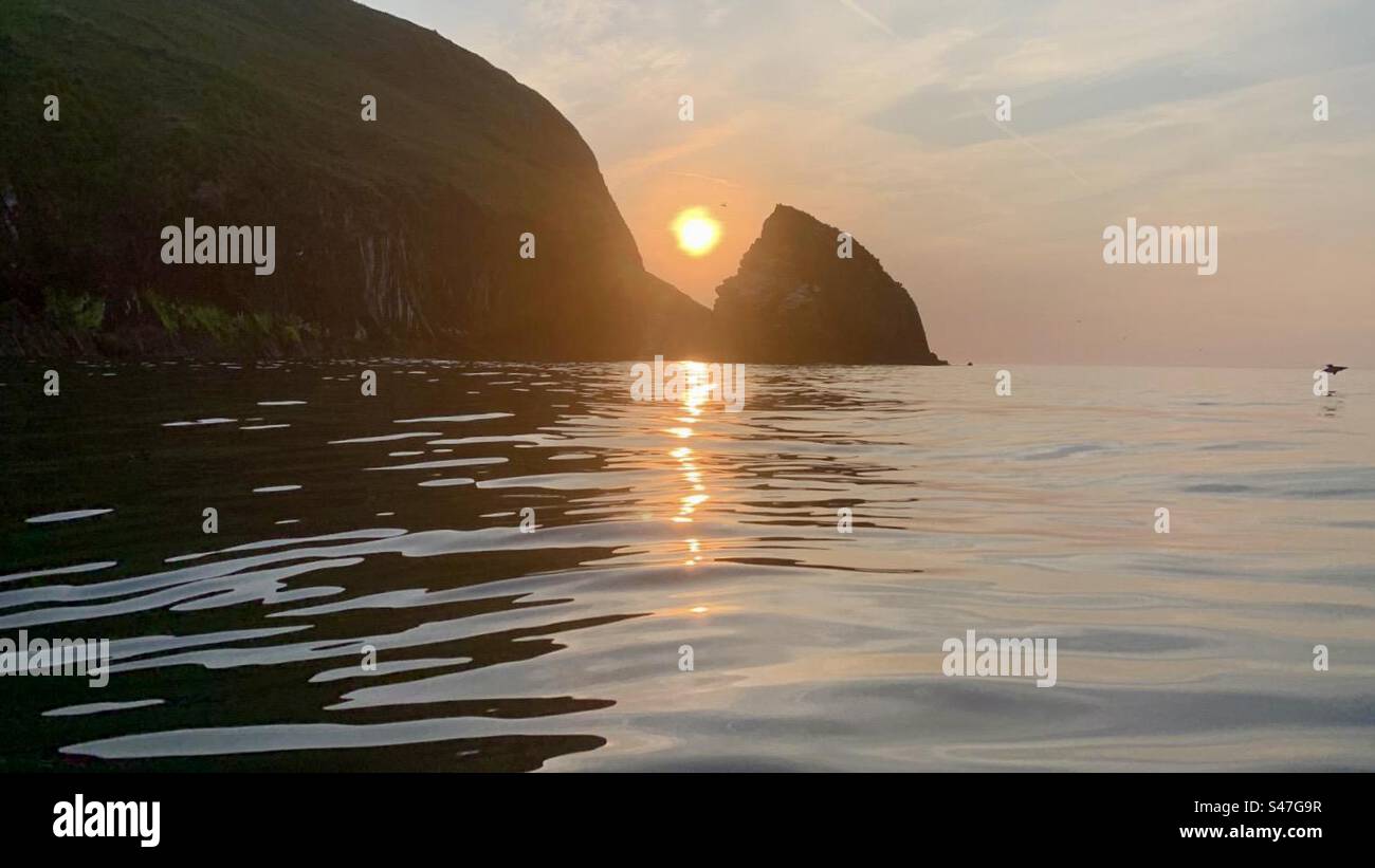 Sun dropping down behind outcrop of rock by the coast Stock Photo - Alamy