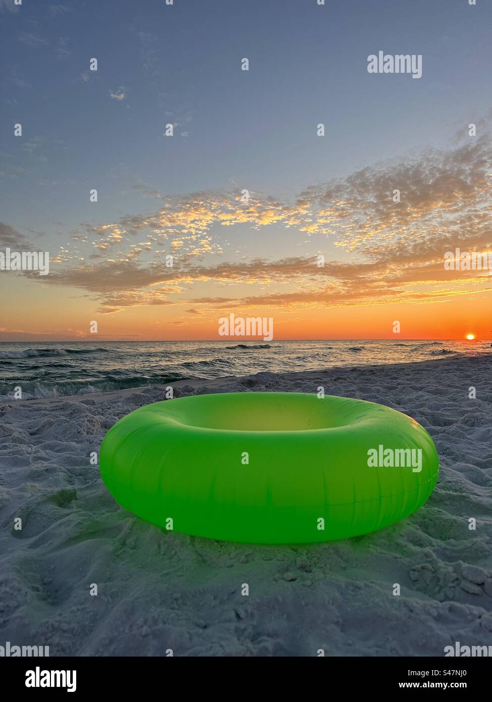 Bright green swim floaty with golden sun setting over the Gulf of ...