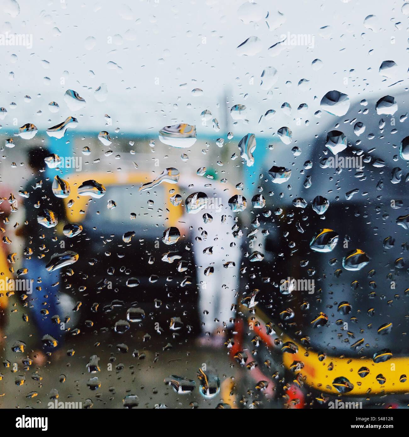 A taxi and an autorickshaw seen through a car window with rain droplets ...