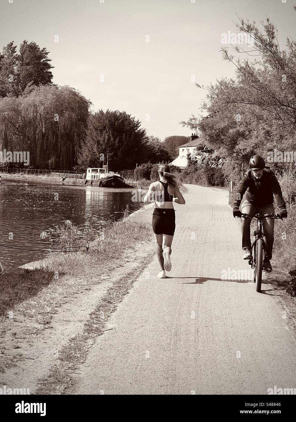 Cyclist and runner passing on the tow path with the Isis pub and ...