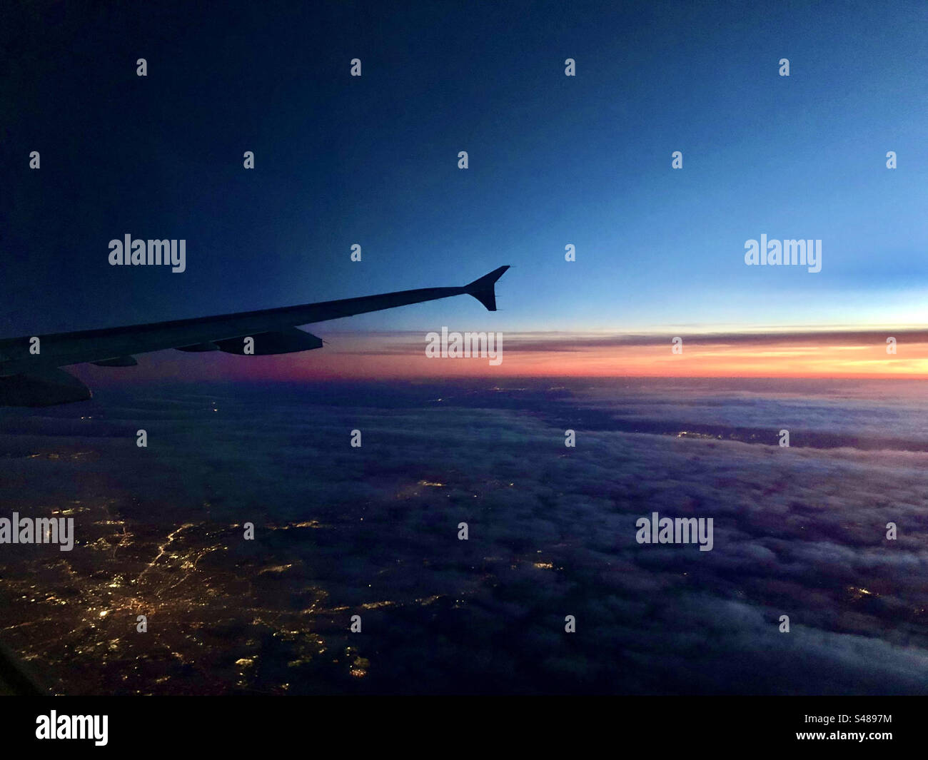 Airbus A321 flying over a city during a sunset. There sky is a mix of ...