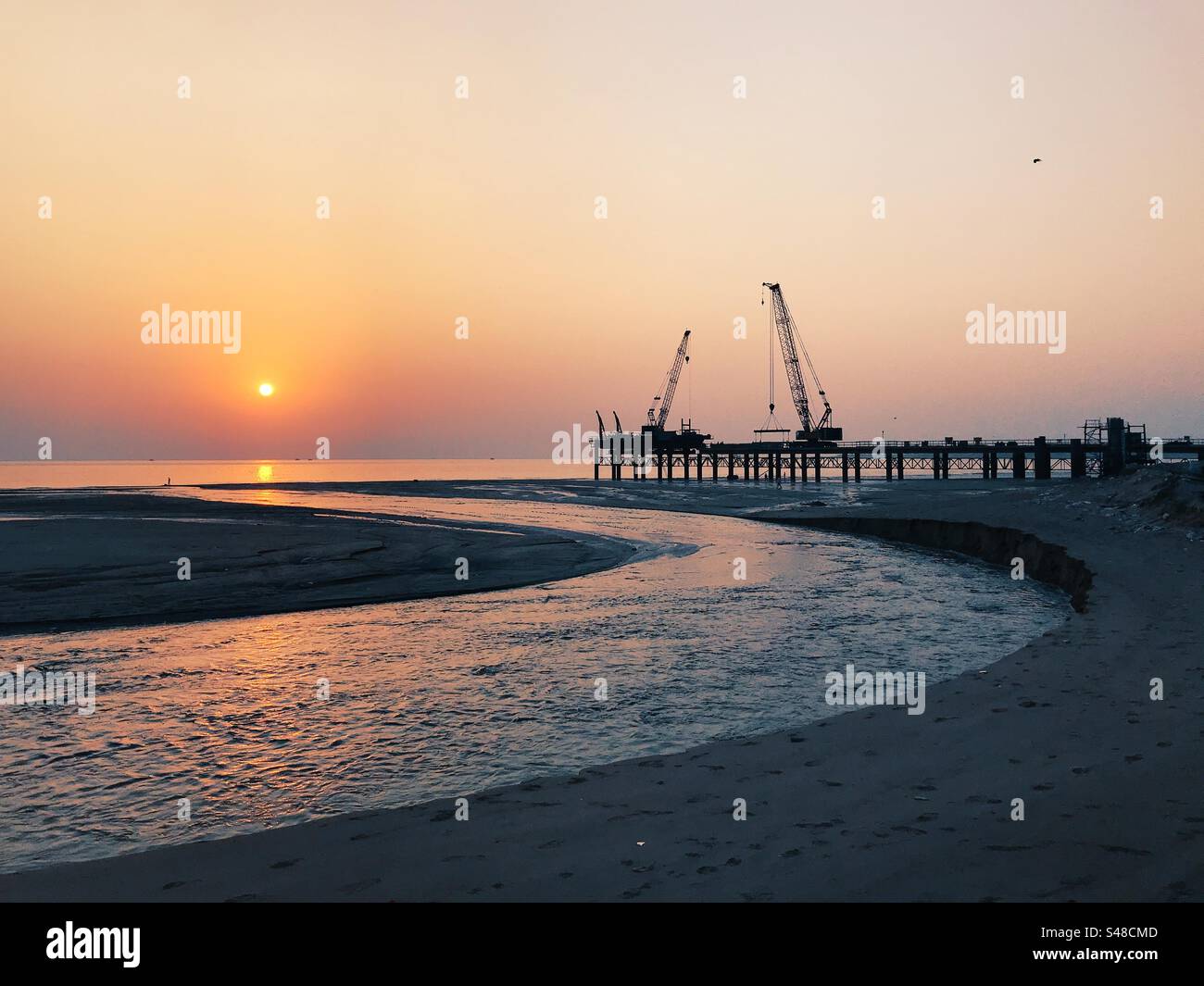 Construction crane and infrastructure on a beach during sunset Stock ...