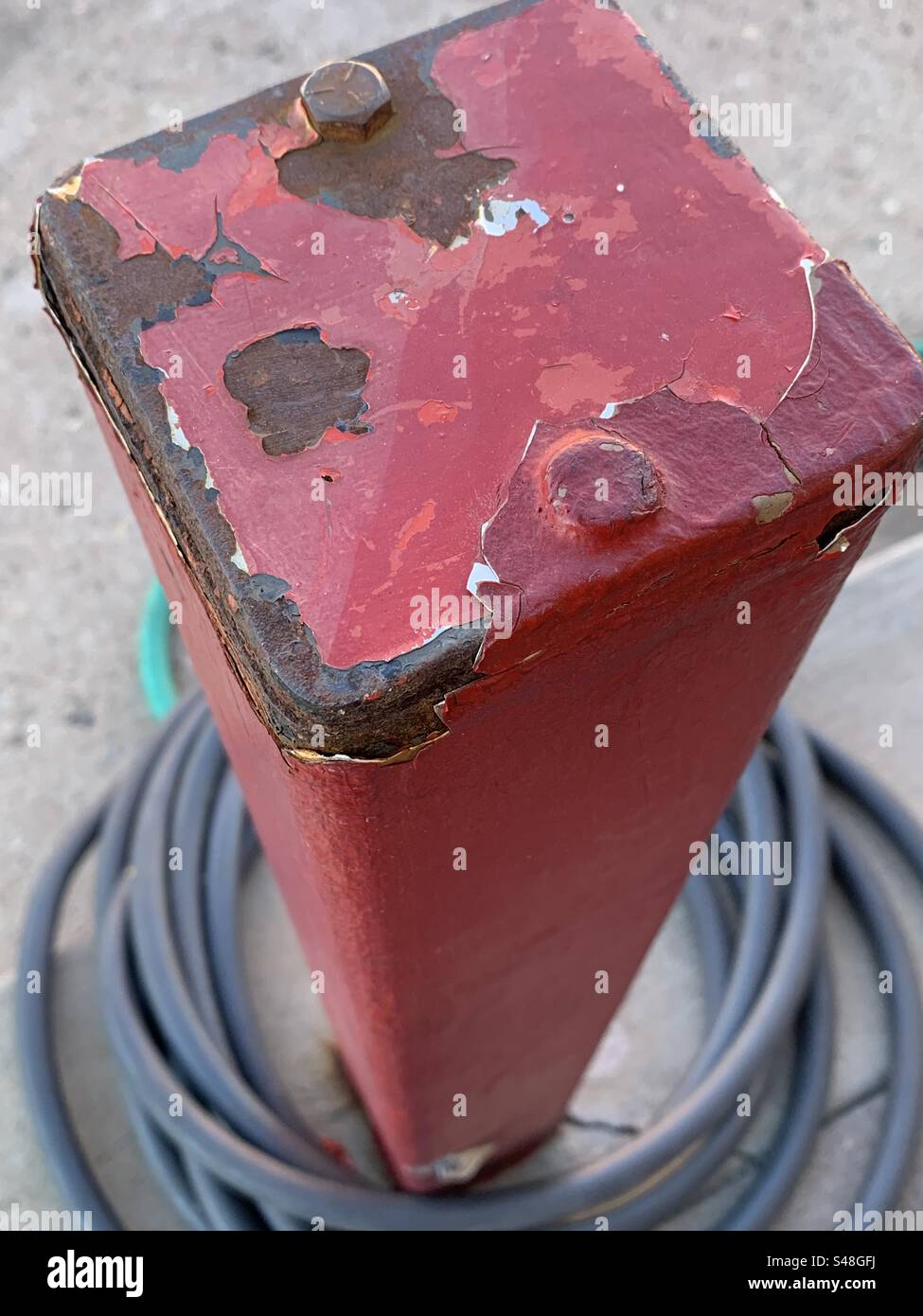 Rusting, chipped red paint off of a post with a gray hose wrapped ...