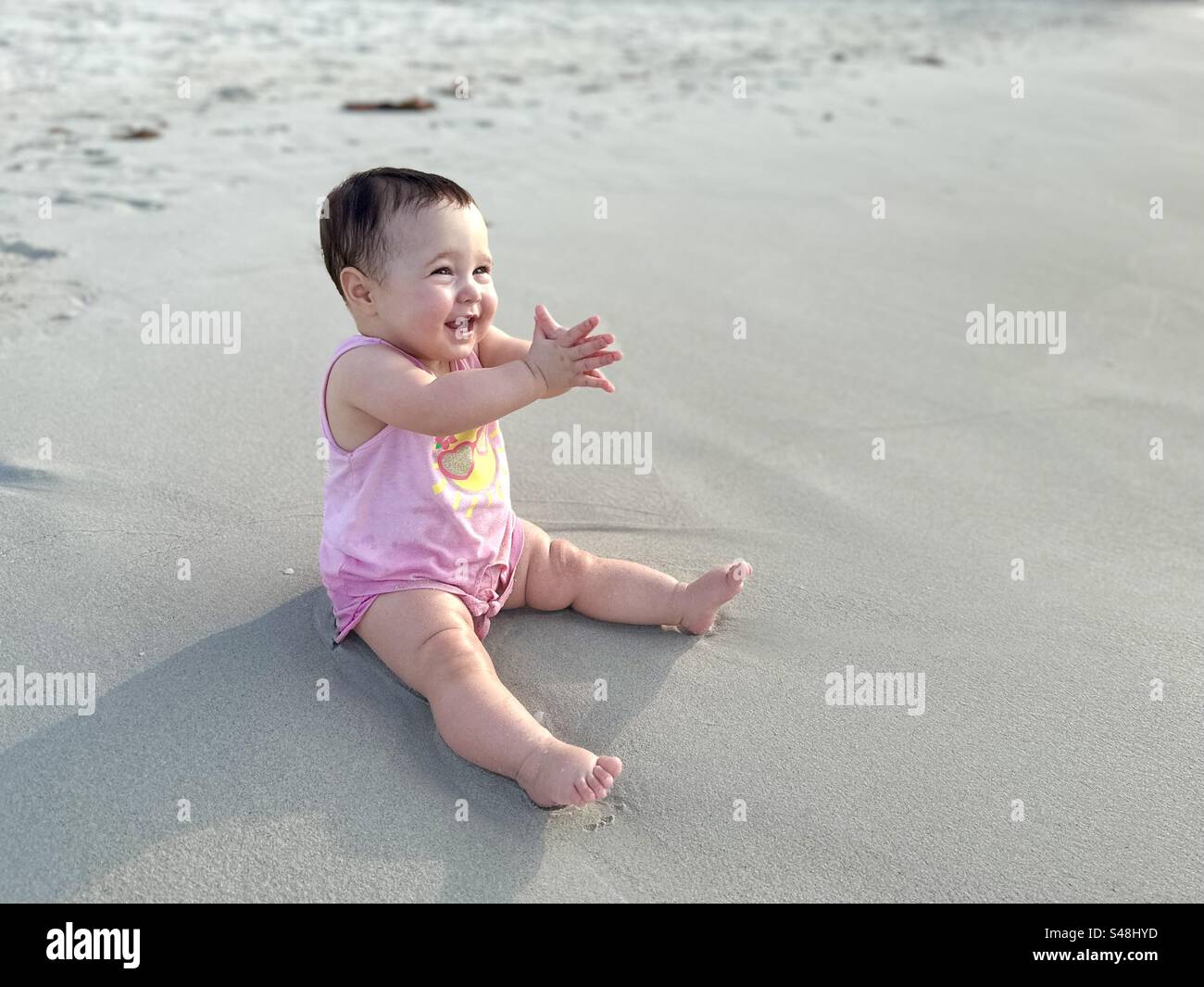 Baby clapping with joy expression sitting on the sand at the beach ...