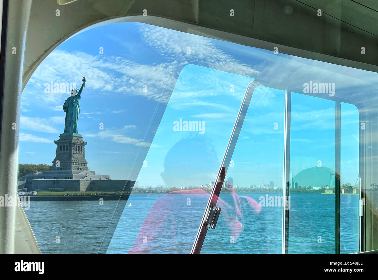 Statue of Liberty through ferry window with figures reflected in glass ...