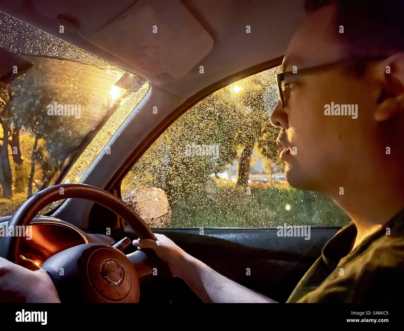 Close-up of a man at the wheel, driving a car on a wet, rainy night ...