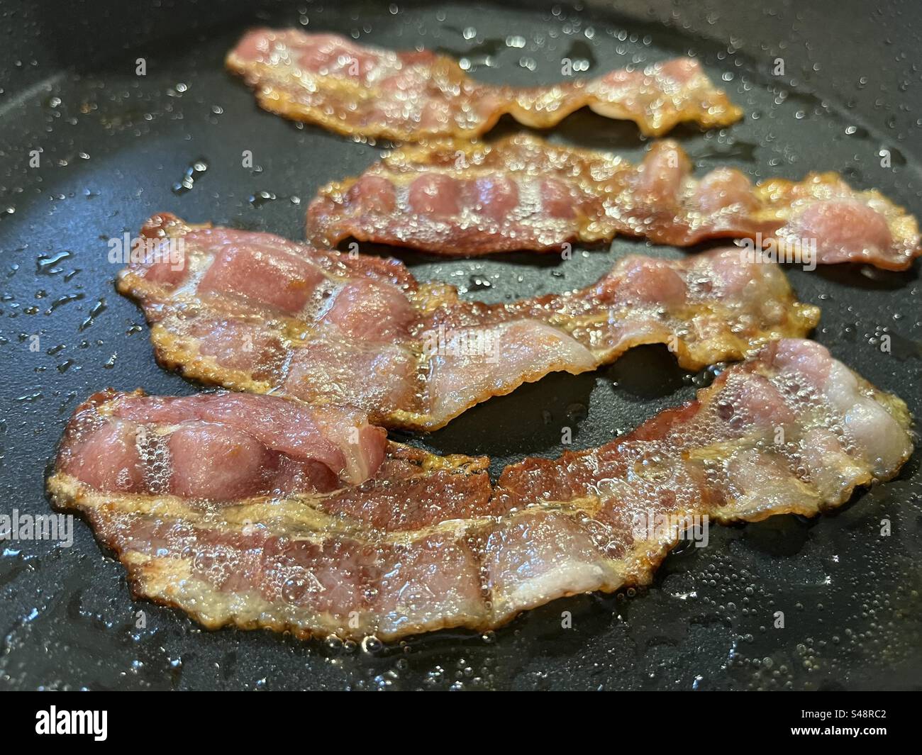 Three slices of juicy bacon that is fried Stock Photo - Alamy