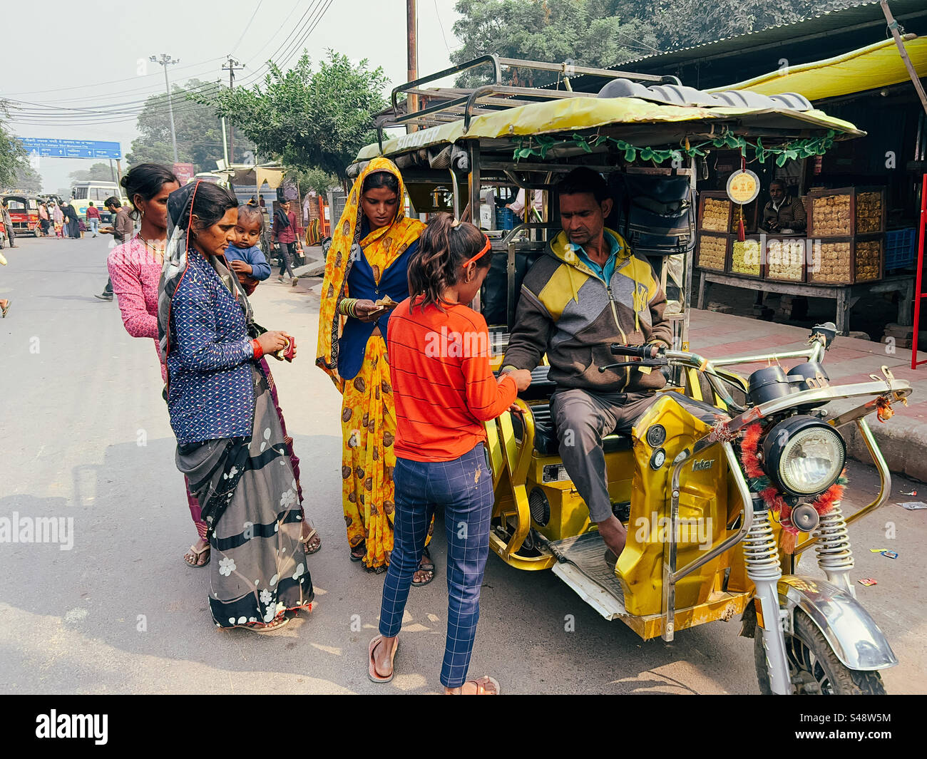 Indian women passengers paying money to an electronic rickshaw driver ...