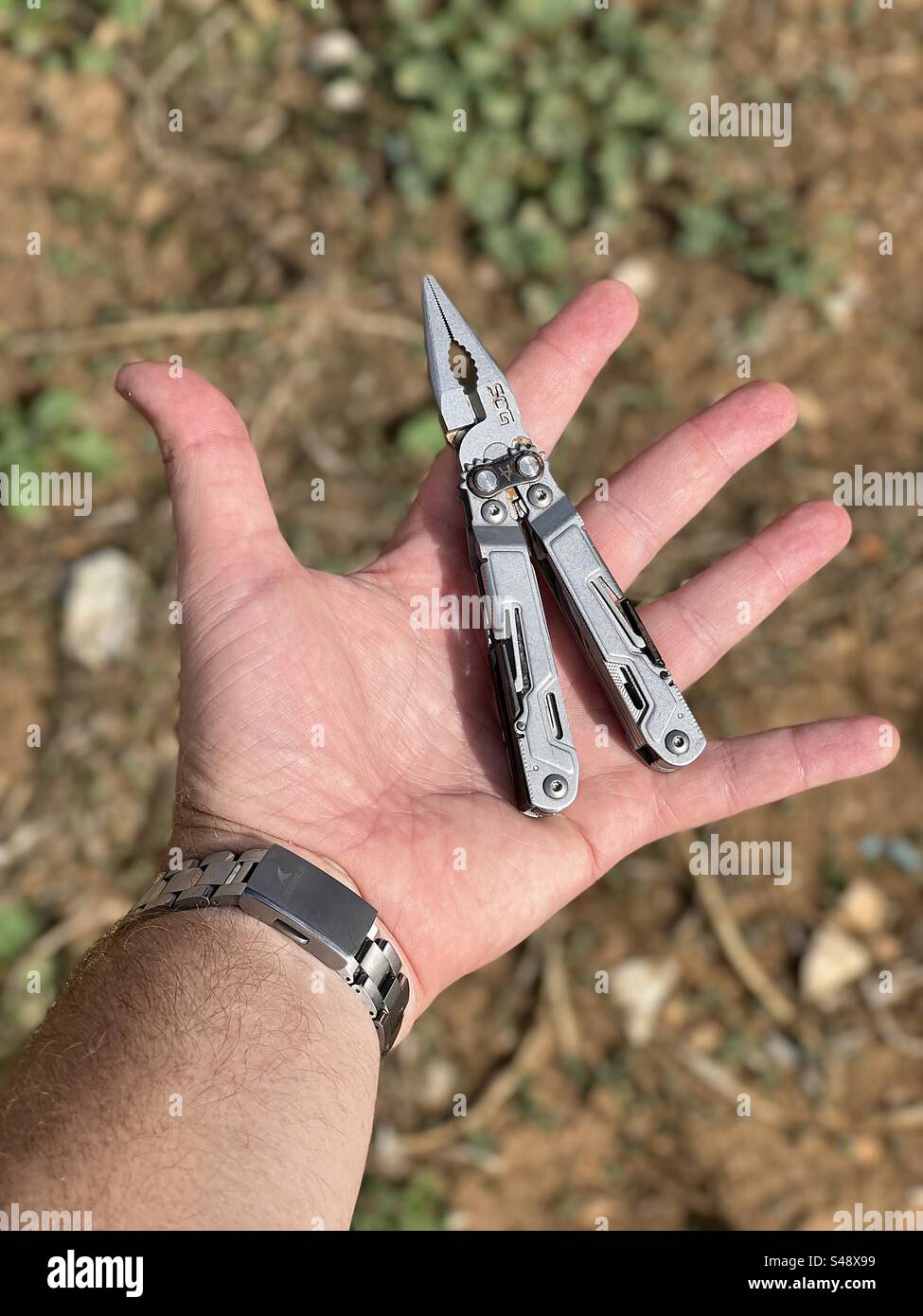 A small multitool pliers placed on an open man hand wearing a stainless ...