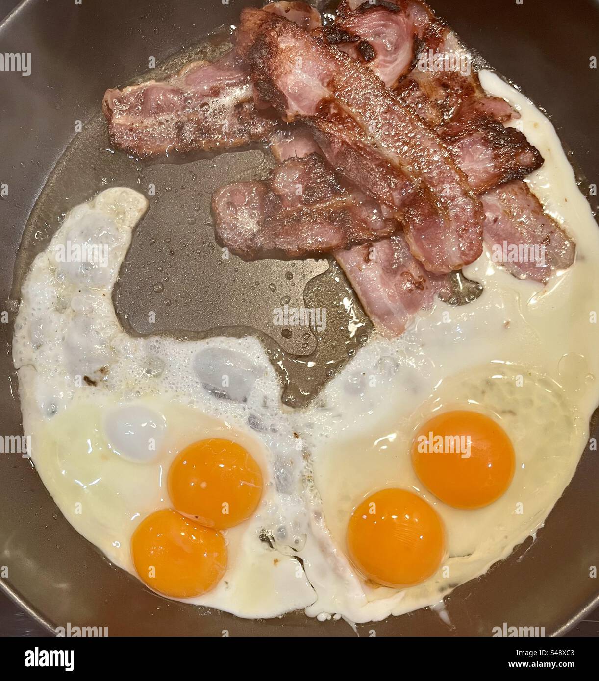 Bacon and two double eggs frying in a pan for a weekend breakfast Stock ...