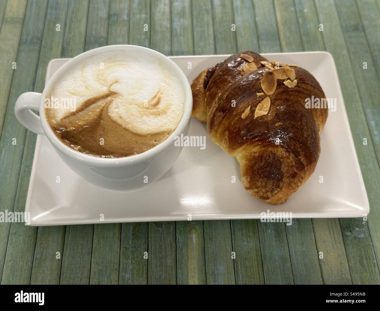 Breakfast at the bar with cappuccino and croissant over a ceramic board ...
