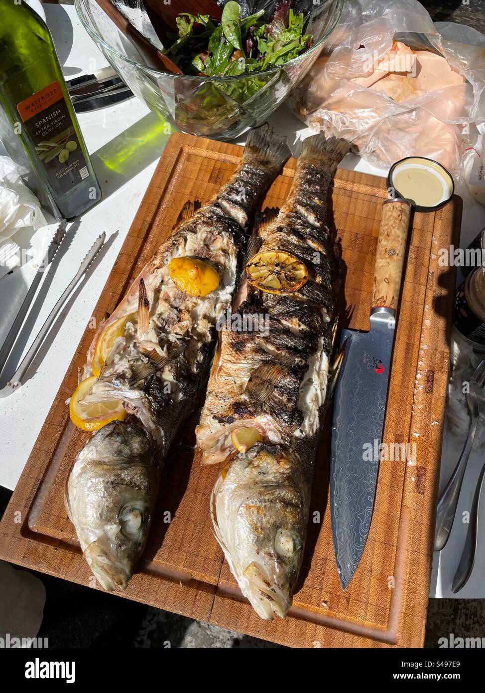 Fish grilled on a barbecue grill resting on a serving board ready for ...