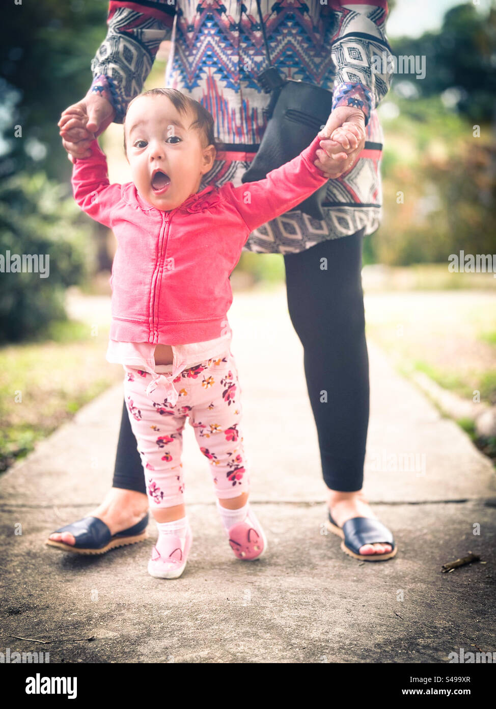 Baby’s first steps outdoors. Baby walking with excitement being helped ...