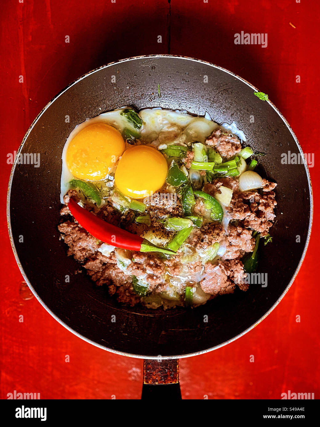 Meat with green hot chilii peppers and two eggs with a red chilli ...