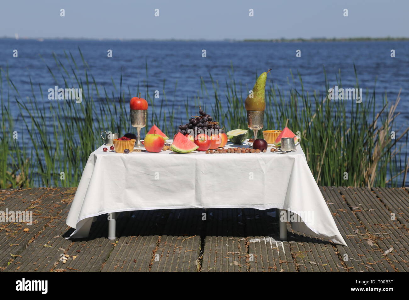 Pick-nick table with fruit, beside a blue lake Stock Photo - Alamy