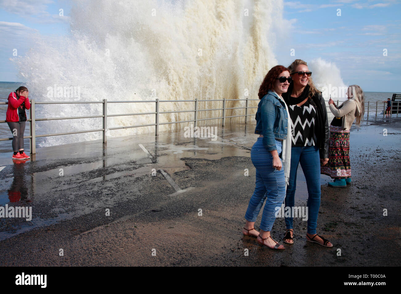 Wave crashing on to pier behind people taking photos Stock Photo - Alamy
