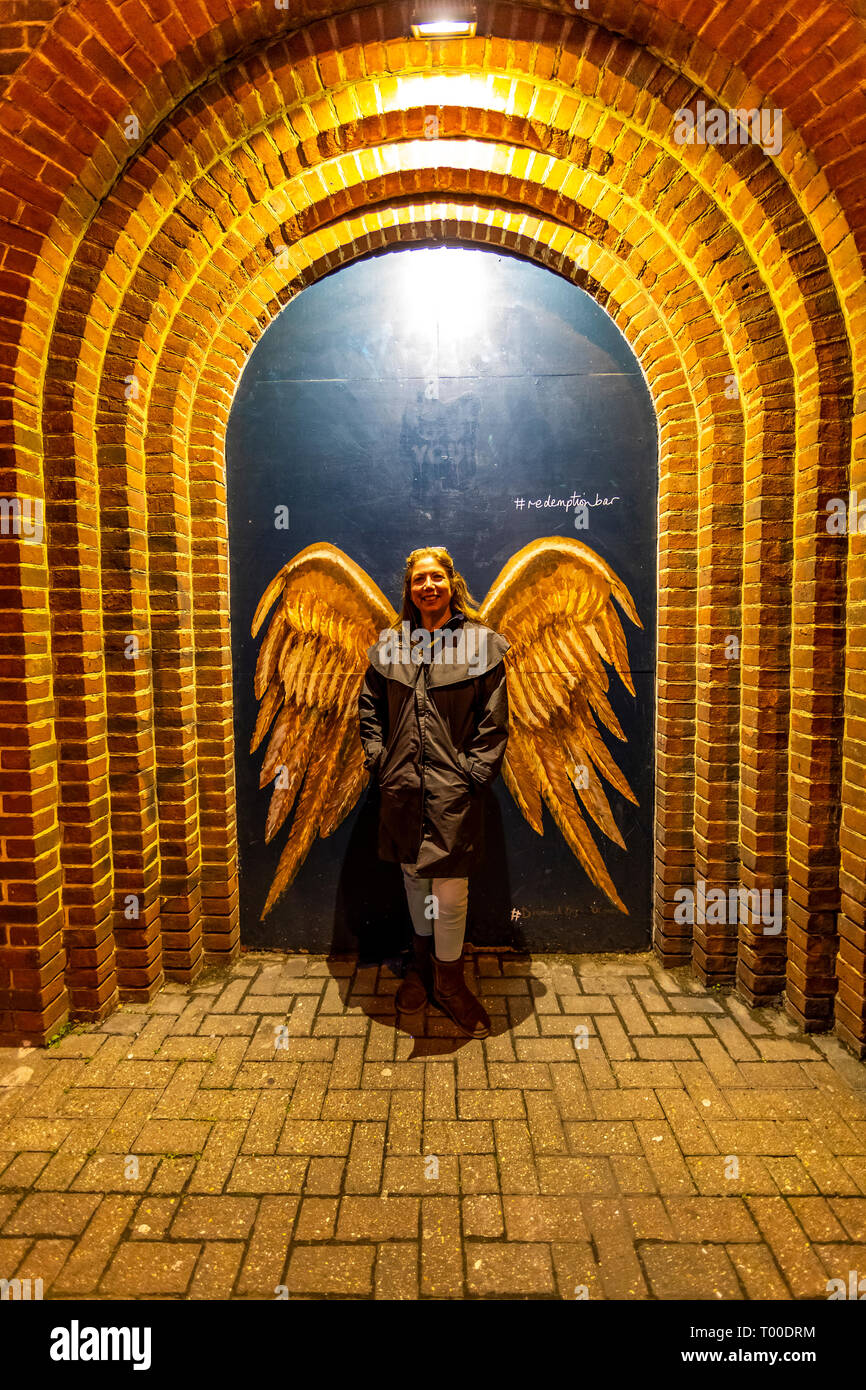 A woman poses as an angel using street art painted on a doorway ...