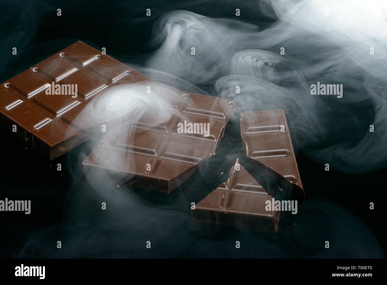 Broken chocolate bar isolated on black in smoke Stock Photo - Alamy