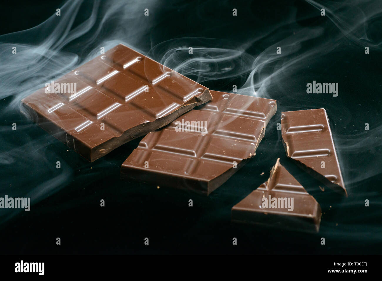 Broken chocolate bar isolated on black in smoke Stock Photo - Alamy