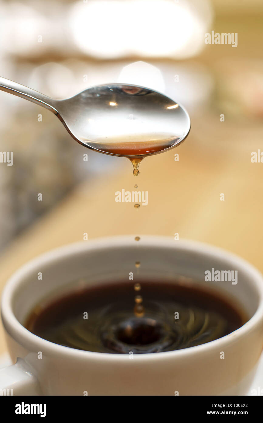 Closeup blob of coffee dripping from metal spoon into mug with coffee ...