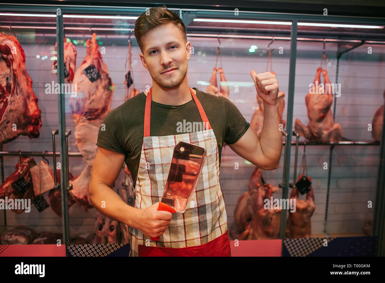 Young man stand and meat shelf in grocery store. He hold butcher knife ...