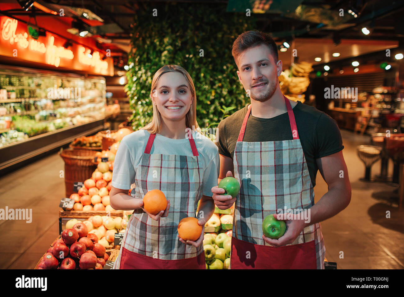 Young man and woman stand at fruit boxes in grocery store. They hold ...