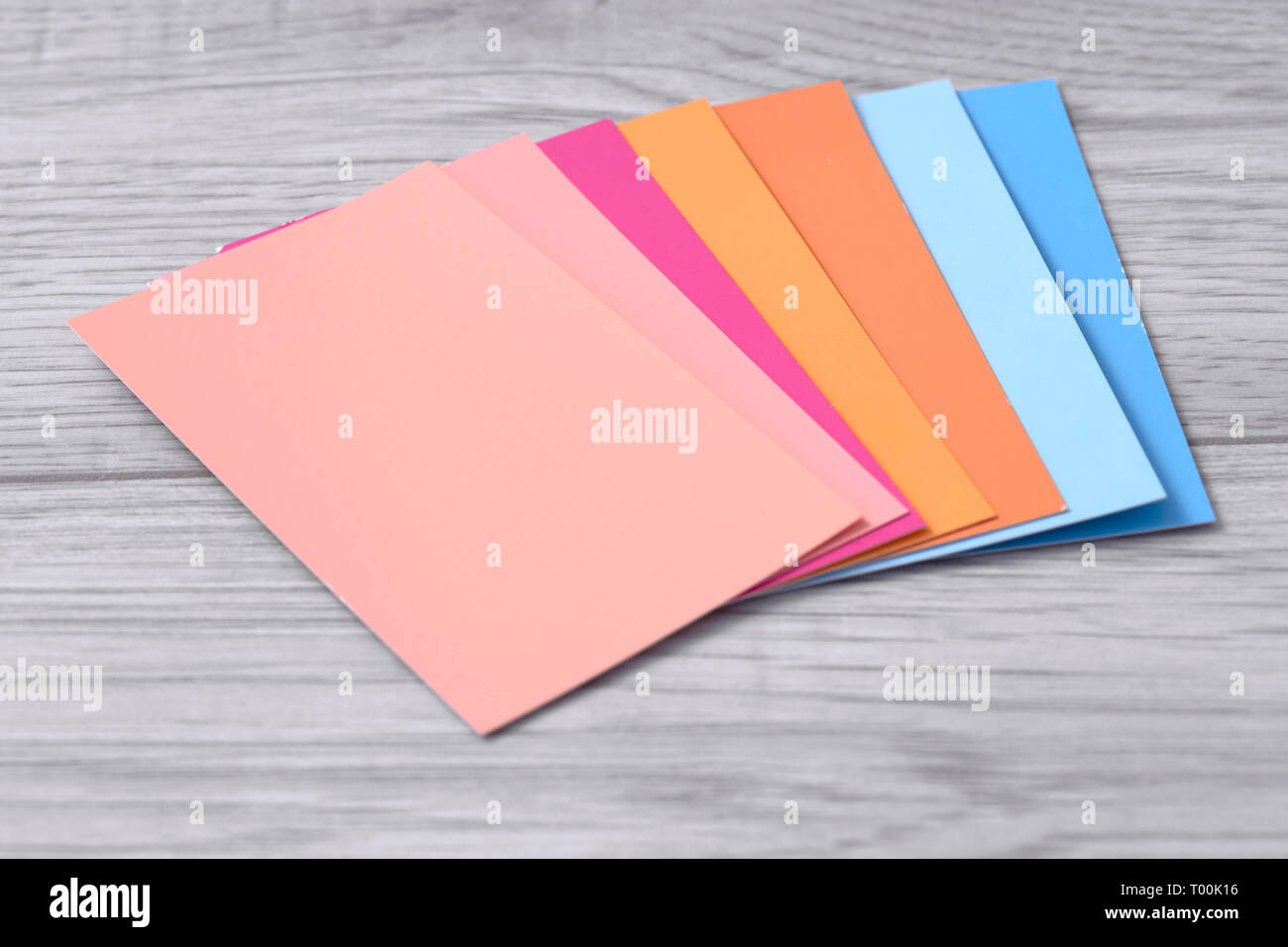 Colour paint swatch cards on a grey wood background with pinks oranges ...