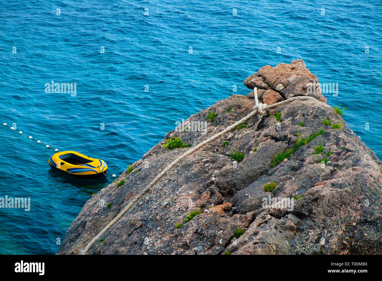 Yellow inflatable boat parked to a large beautiful rock on seaside ...