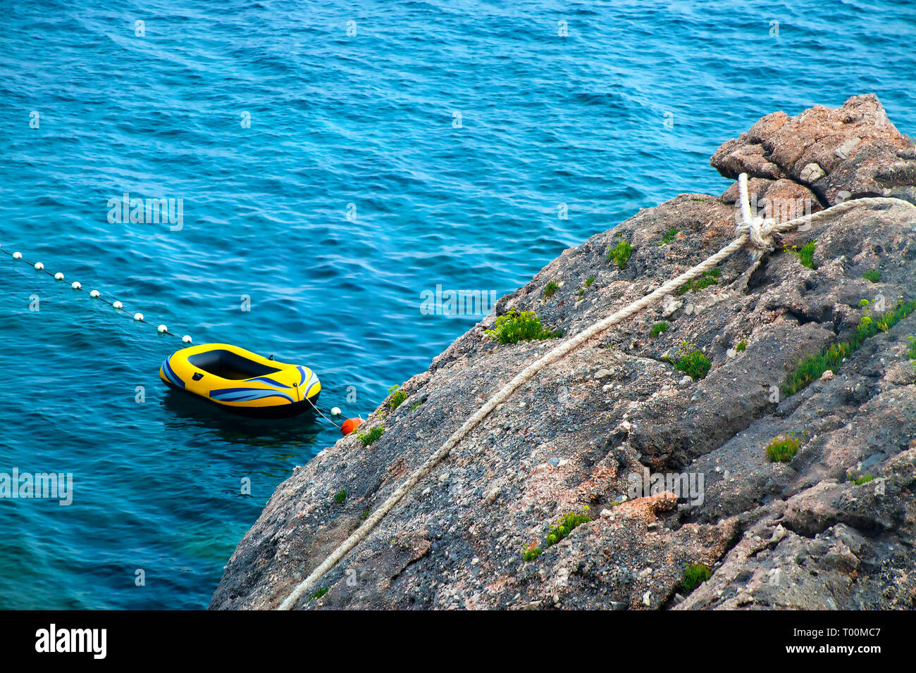 Large rock at seaside with inglatable boat under it and buoy chain ...