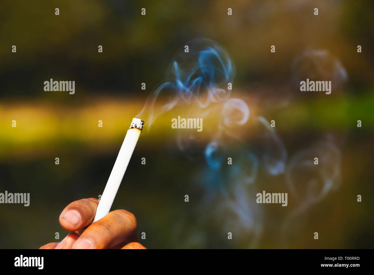 Hand holding a cigarette with smoke Stock Photo - Alamy