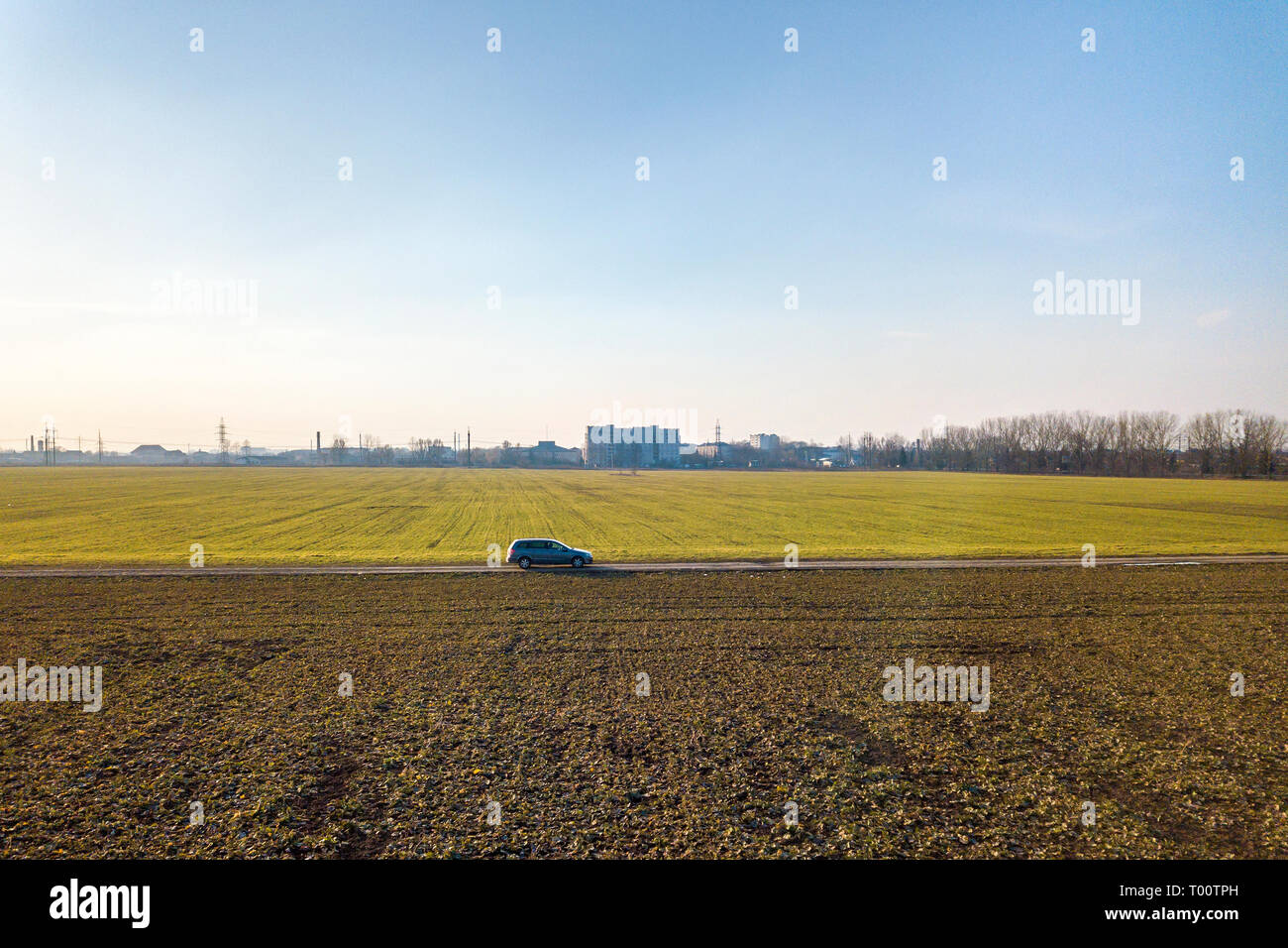 Aerial view of car driving by straight ground road through green fields ...