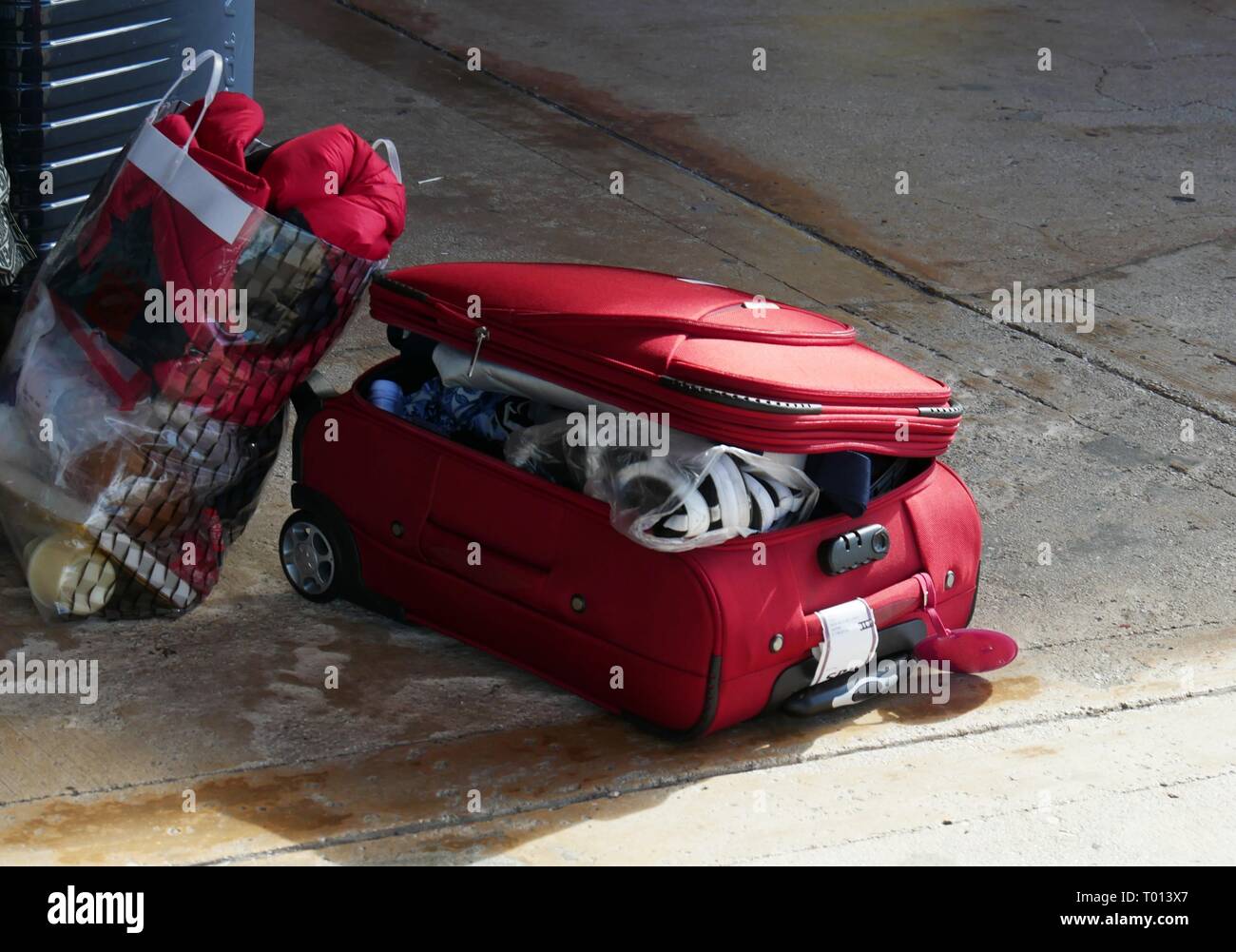 A red luggage bag and a plastic bag both open, on the ground of an ...