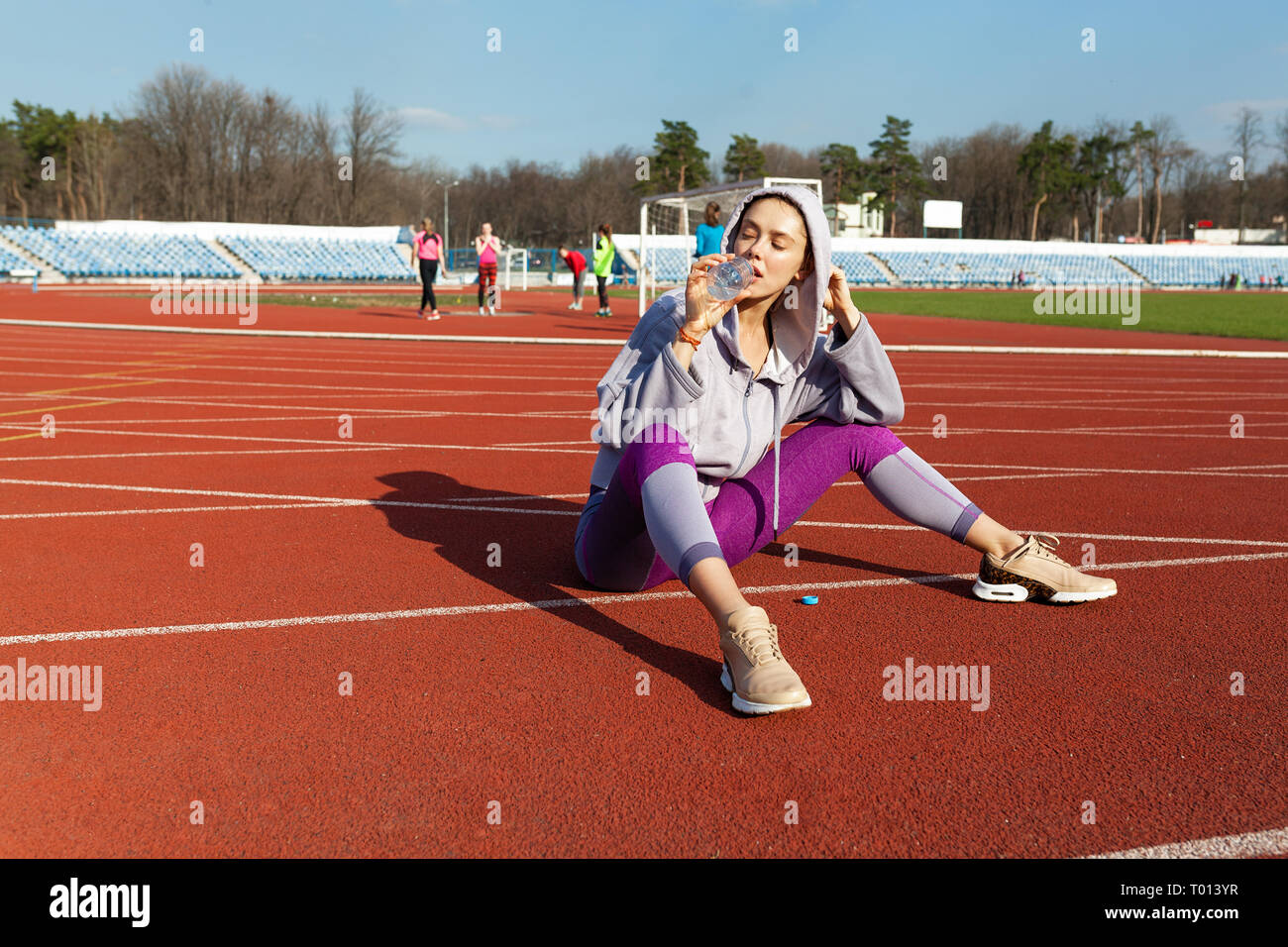 Fit sporty girl relaxing after jogging, sitting on the running track at ...