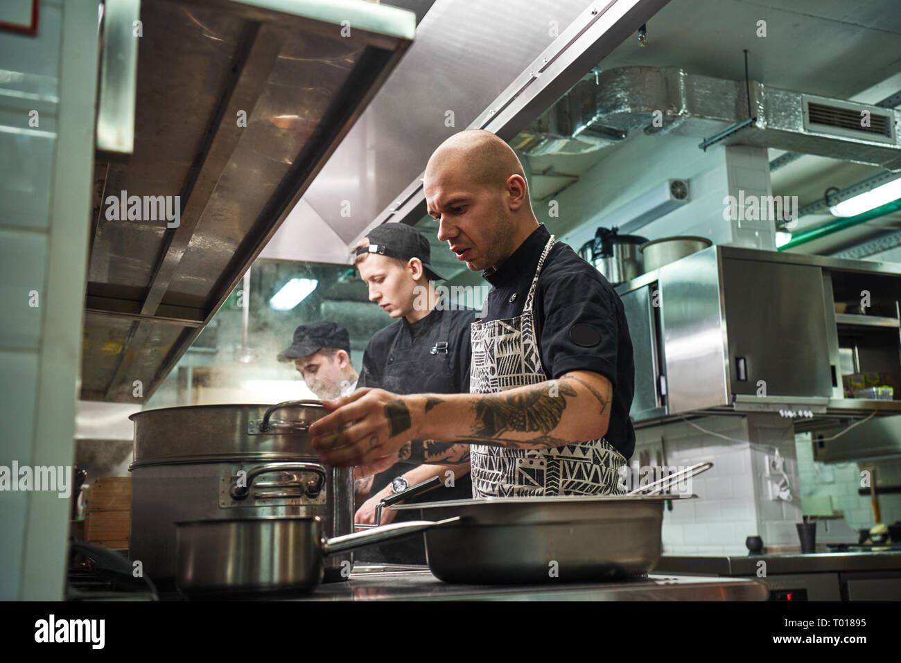 Professional team. Concentrated chef in apron, with tattoos on his arms ...