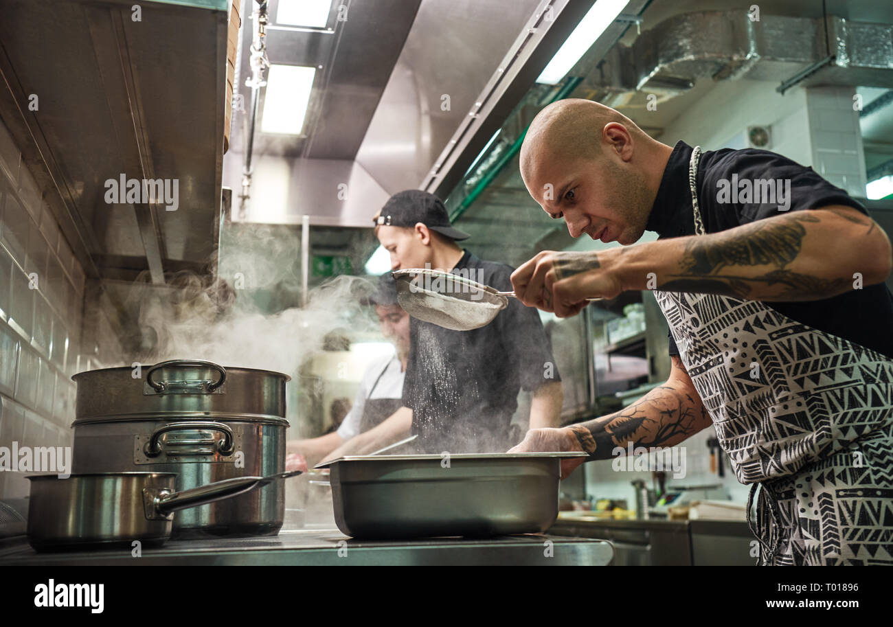 Restaurant kitchen. Professional chef in apron, with tattoos on his ...