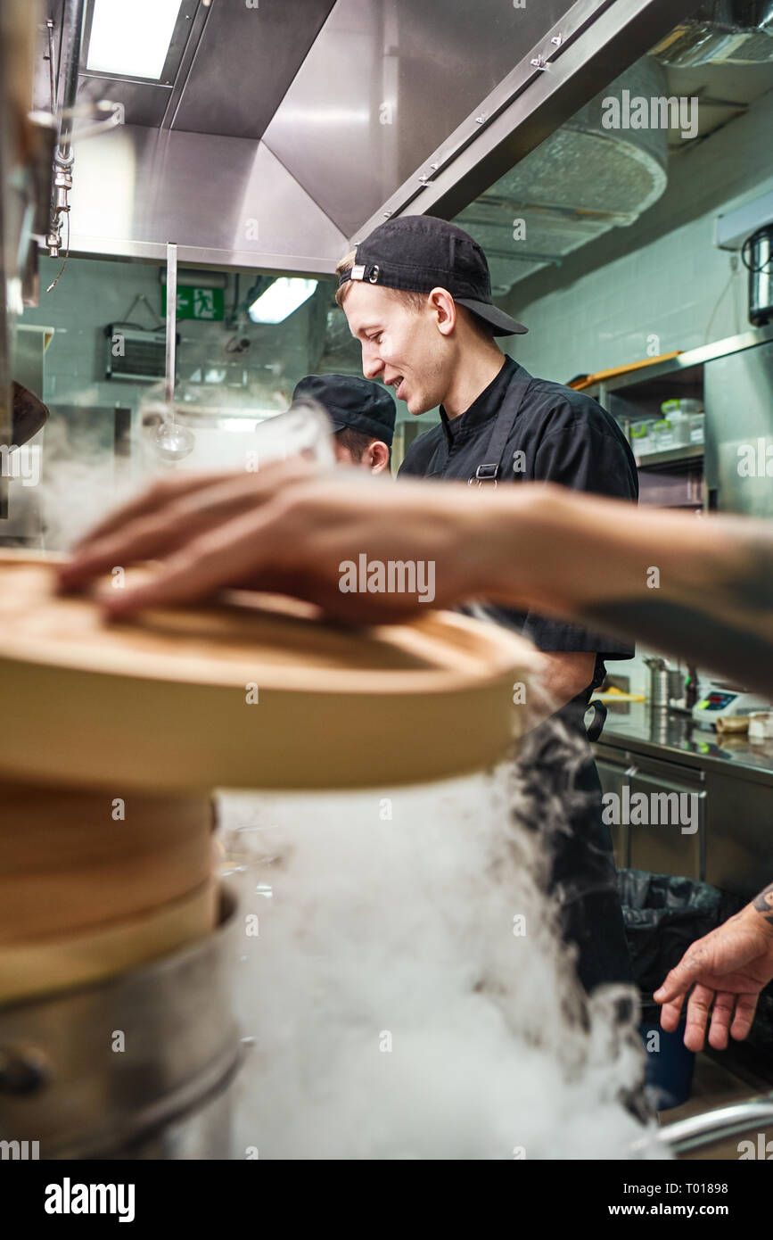 Cooking process. Close up of chef's hand holding wooden lid while ...